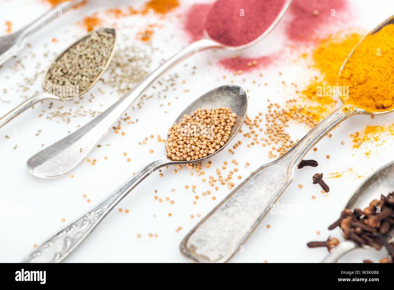 close up view of various bright spices in silver vintage spoons on ...