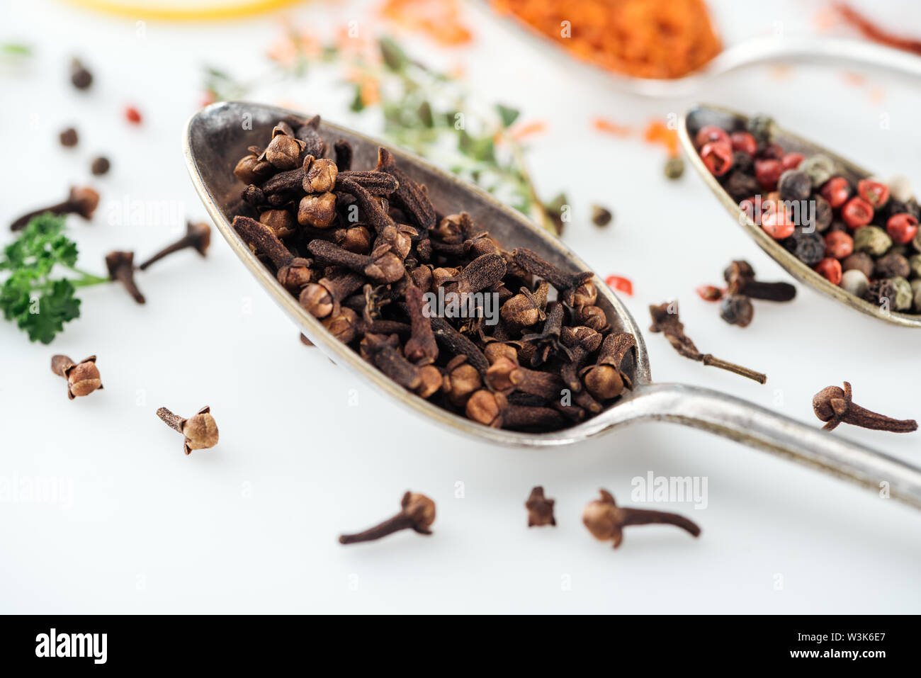 close up view of dry carnation and pepper in silver spoon on white ...
