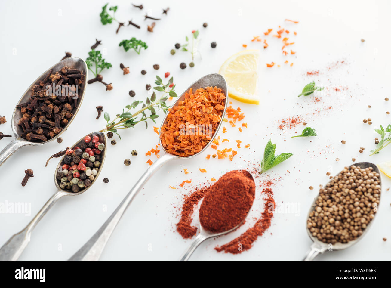 close up view of indian bright spices in silver spoons near herbs on ...