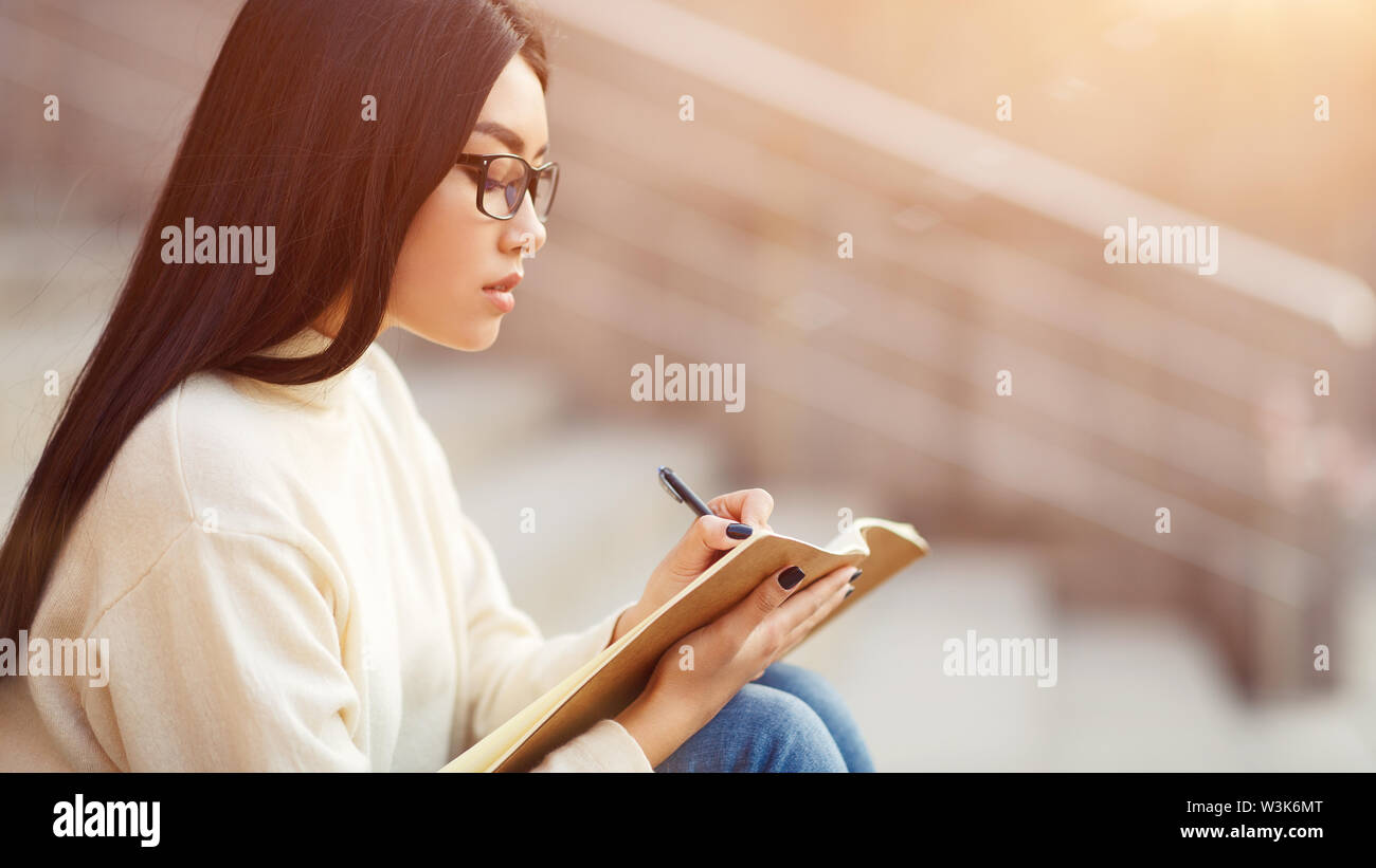 Asian student writing notes in notepad, sitting on city stairs Stock ...