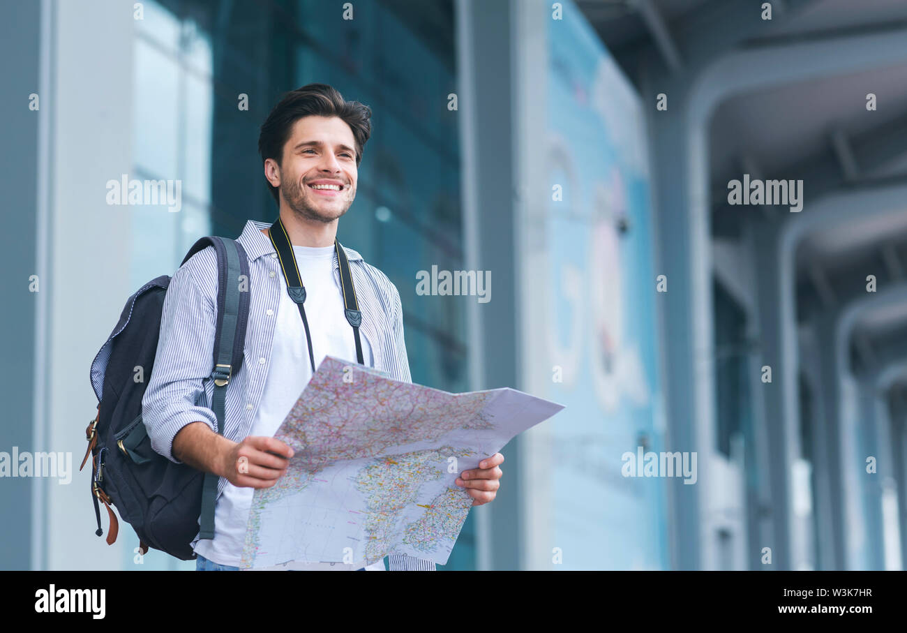 Cheerful man traveler holding map, studying new destinations at airport ...