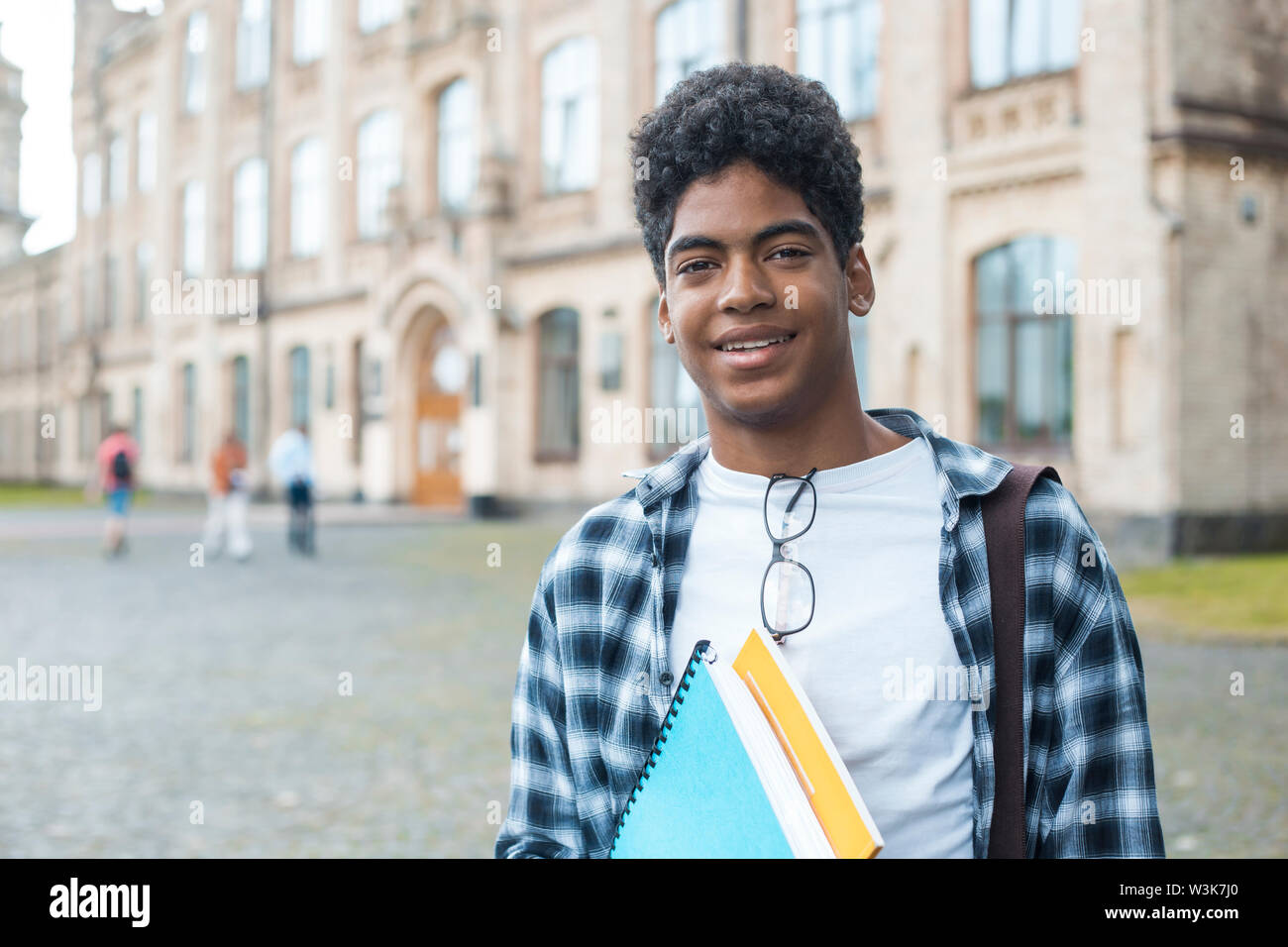 Smiling African American student with glasses and with books near ...