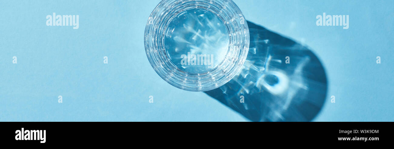top view of glass with clear water on blue background with shadow ...