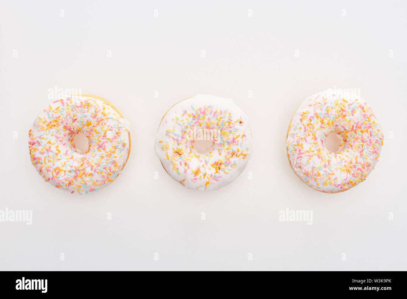 top view of glazed white doughnuts with sprinkles on white background ...
