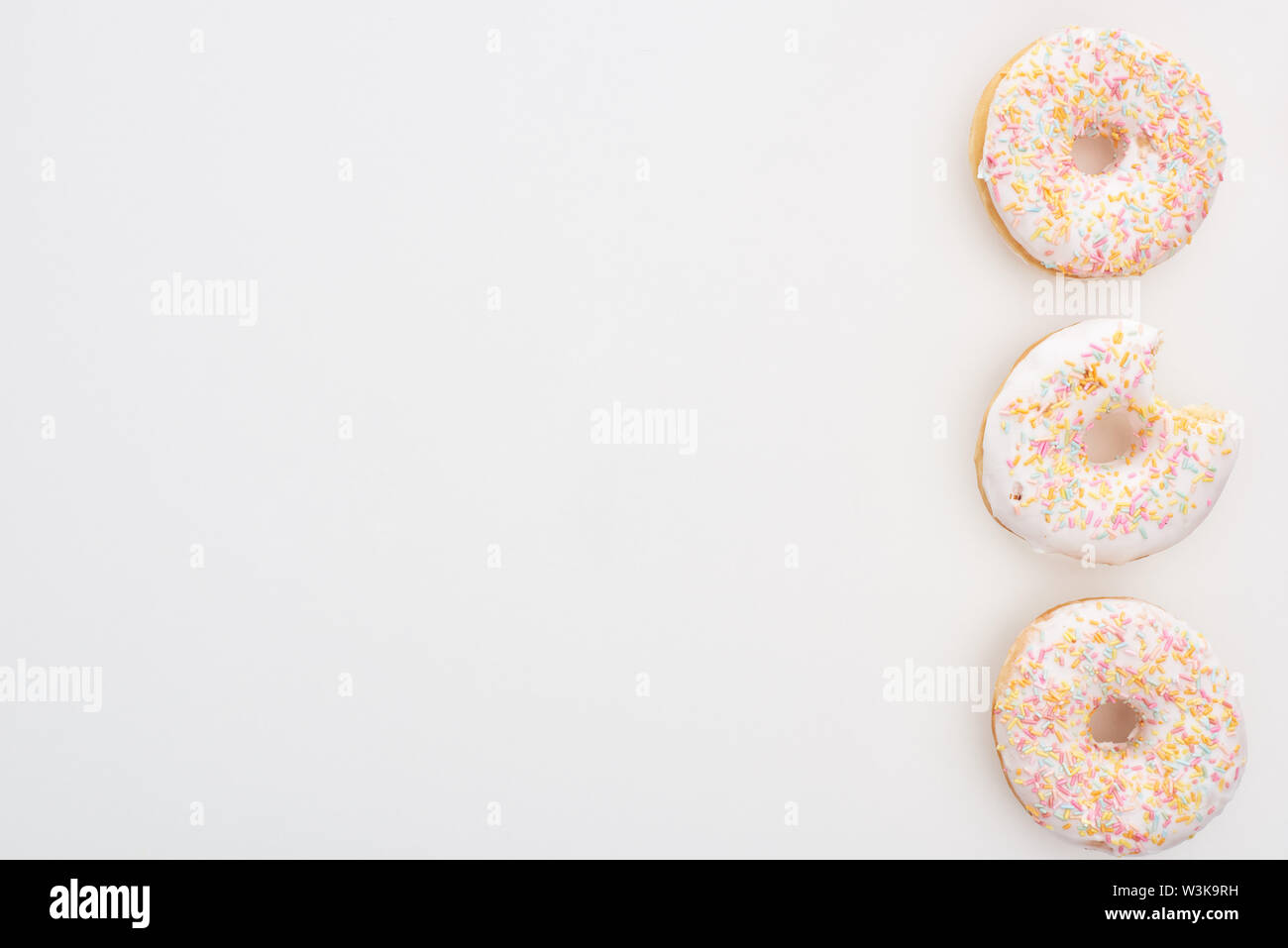 top view of whole doughnuts with sprinkles near bitten one on white ...