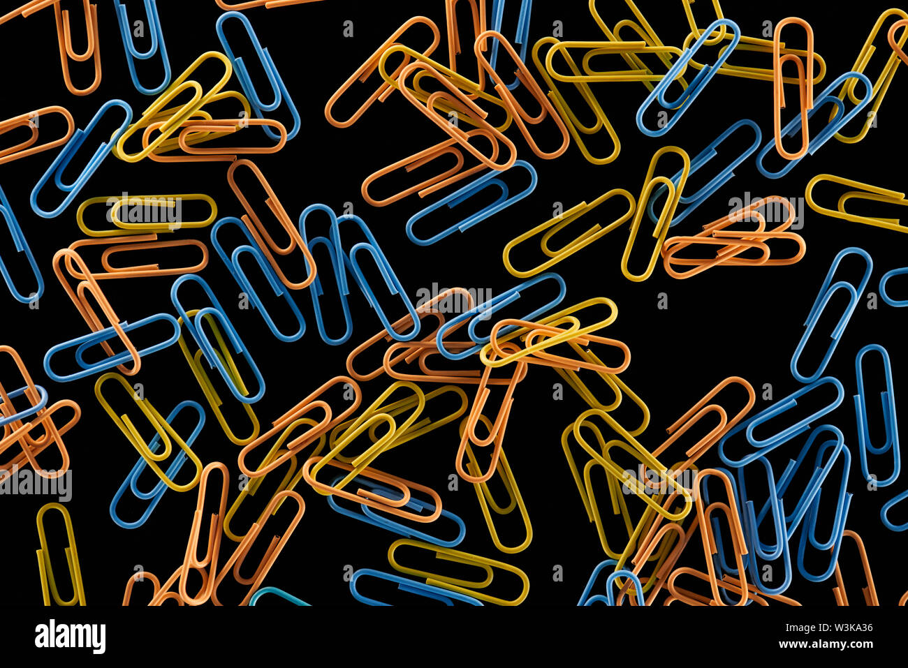 top view of small yellow, orange and blue paper clips isolated on black ...