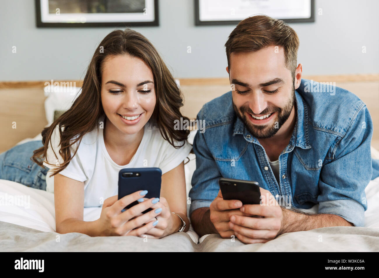 Beautiful young couple in love at home, laying in bed, using mobile ...