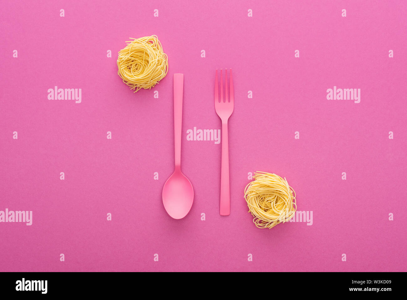 pink plastic fork and spoon upside down near vermicelli pasta on pink ...
