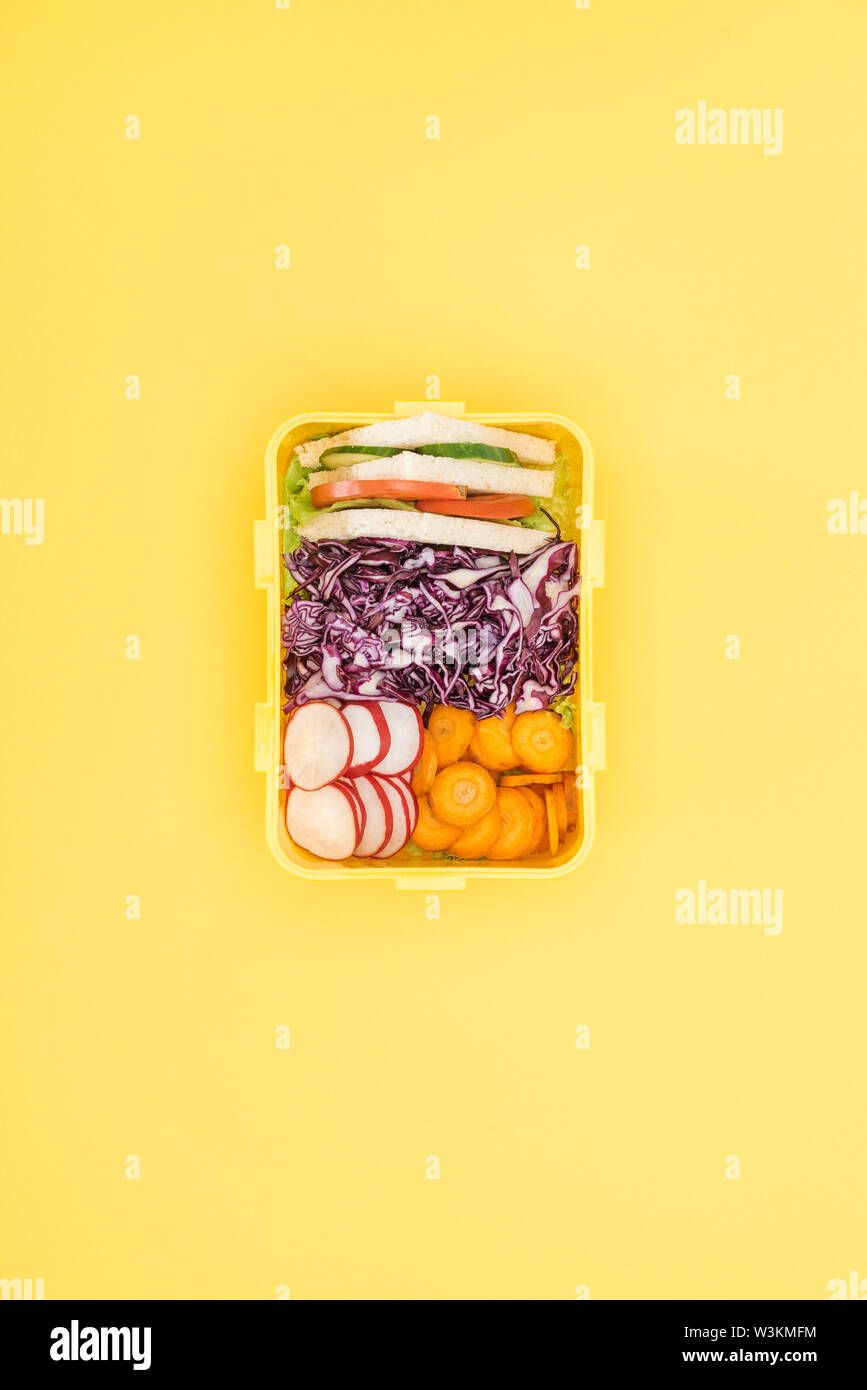 top view of lunch box with sandwiches and vegetables on yellow ...