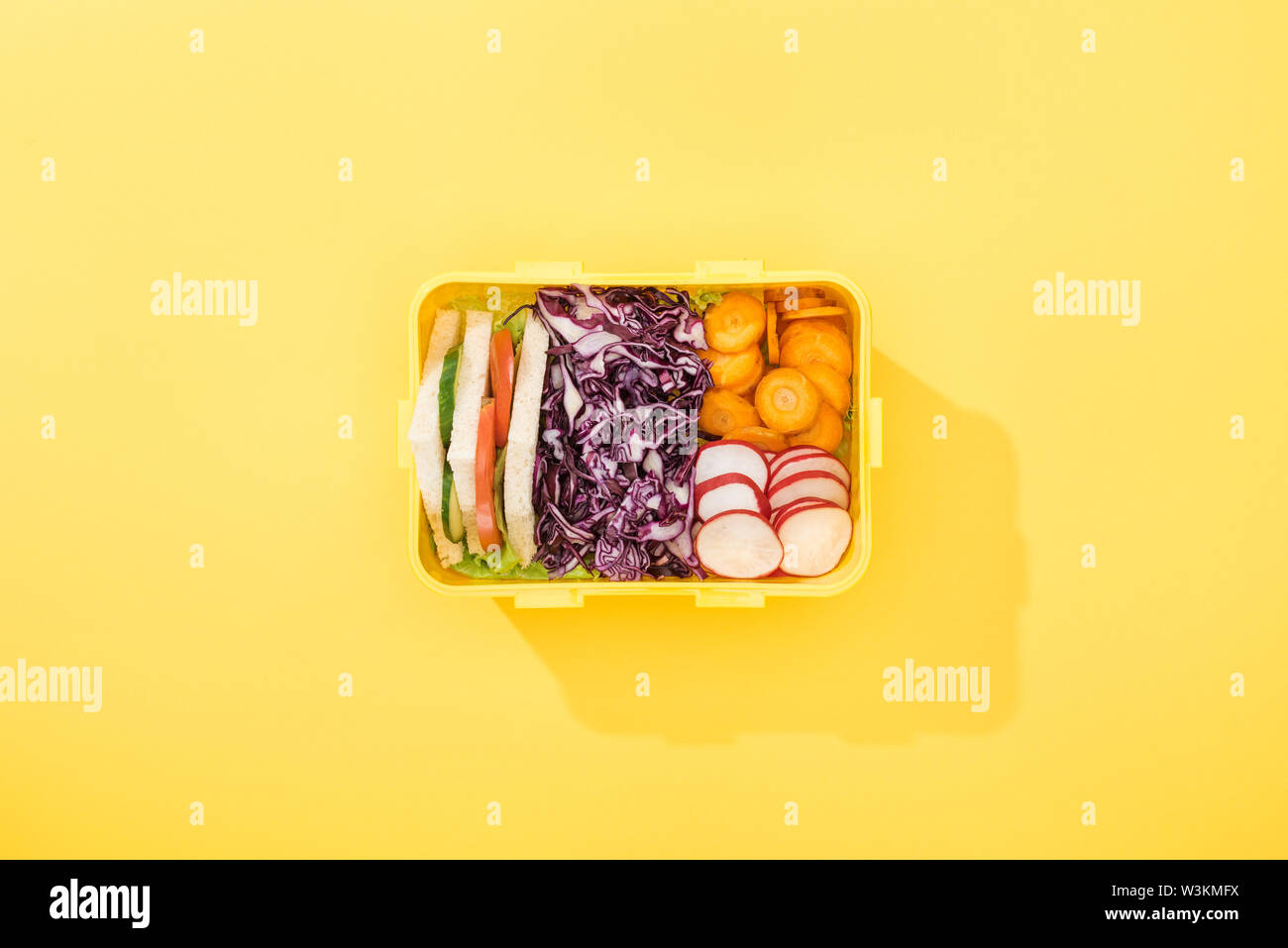 top view of lunch box with sandwiches and vegetables on yellow ...