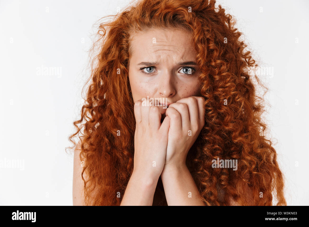 Portrait of an attractive scared young woman with long curly red hair ...