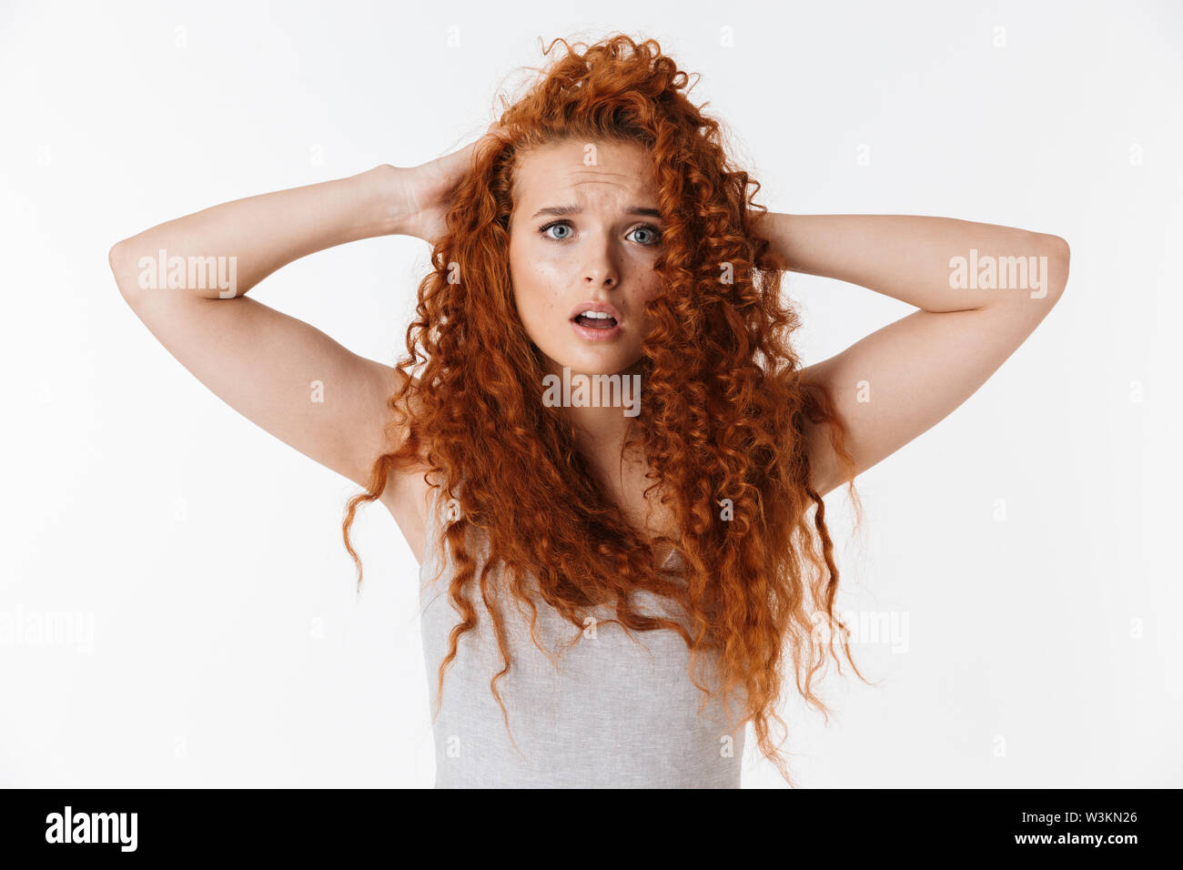 Portrait of an attractive confused young woman with long curly red hair ...