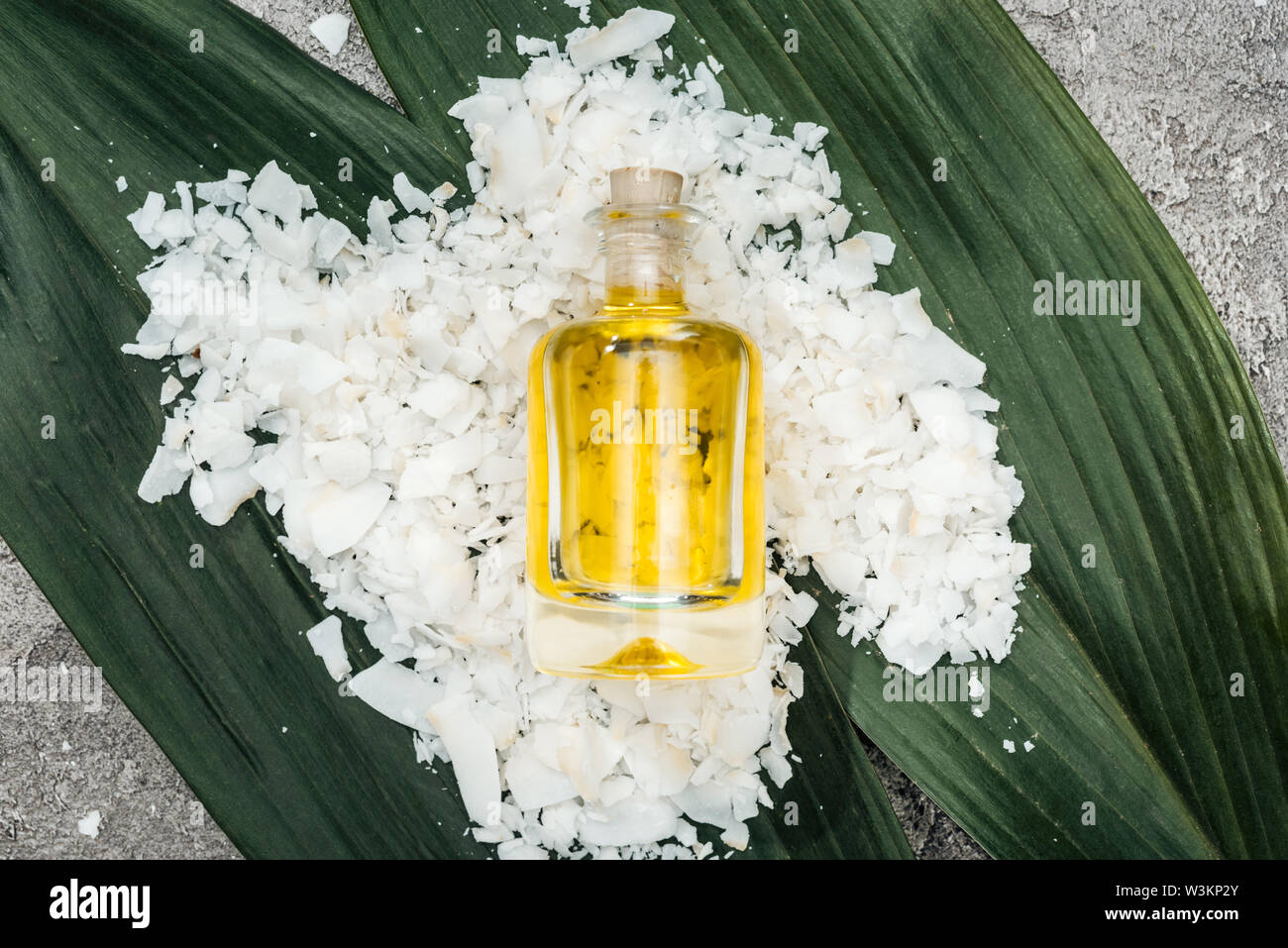 top view of coconut oil in bottle on coconut shaving and palm leaves on ...