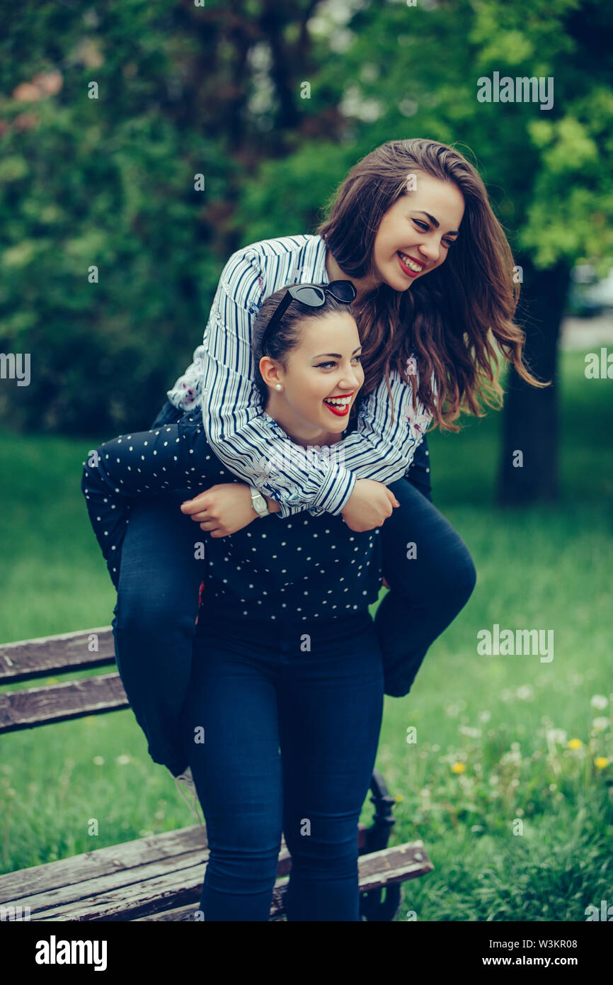 Outdoor shot of young woman carrying her female friend on her back. Two ...