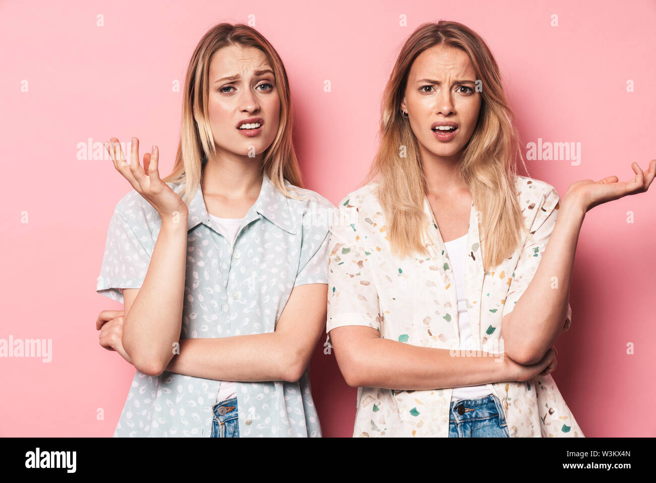 Two attractive confused young girls standing isolated over pink ...