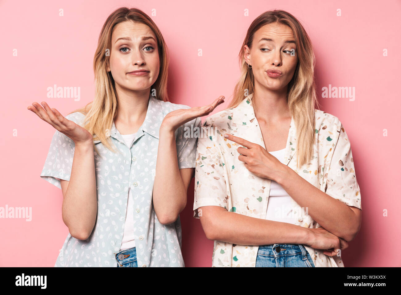 Two attractive confused young girls standing isolated over pink ...