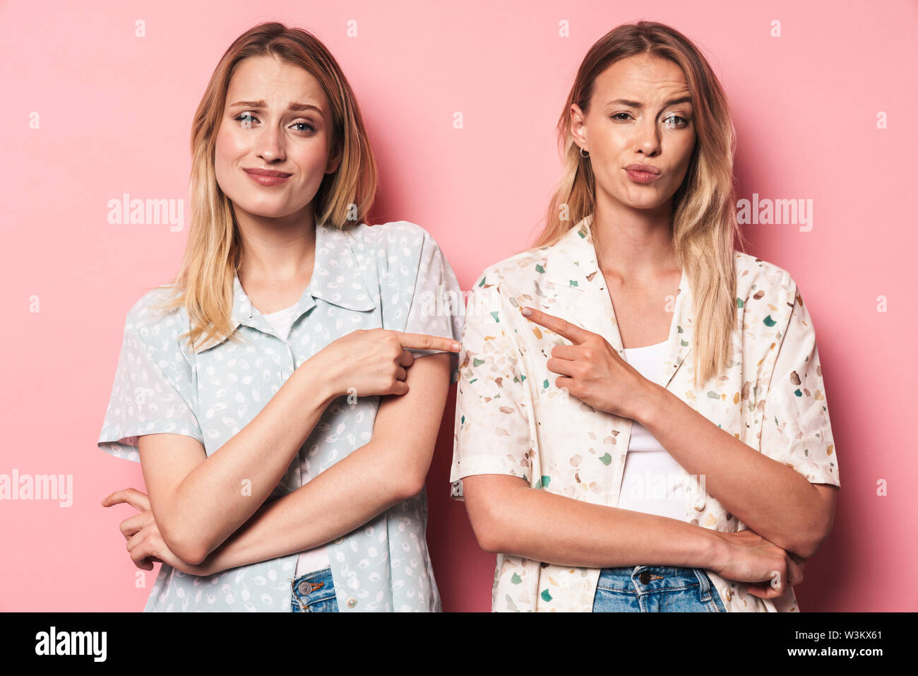 Two attractive confused young girls standing isolated over pink ...