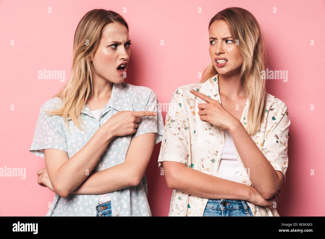 Two attractive confused young girls standing isolated over pink ...