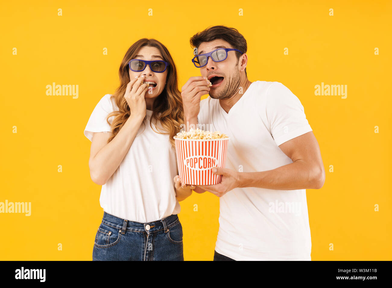 Portrait of shocked couple man and woman in 3D glasses being scared while standing together with ...