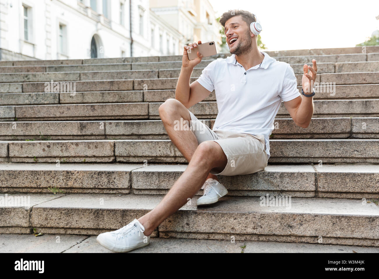 Portrait of happy young man wearing headphones holding smartphone and ...