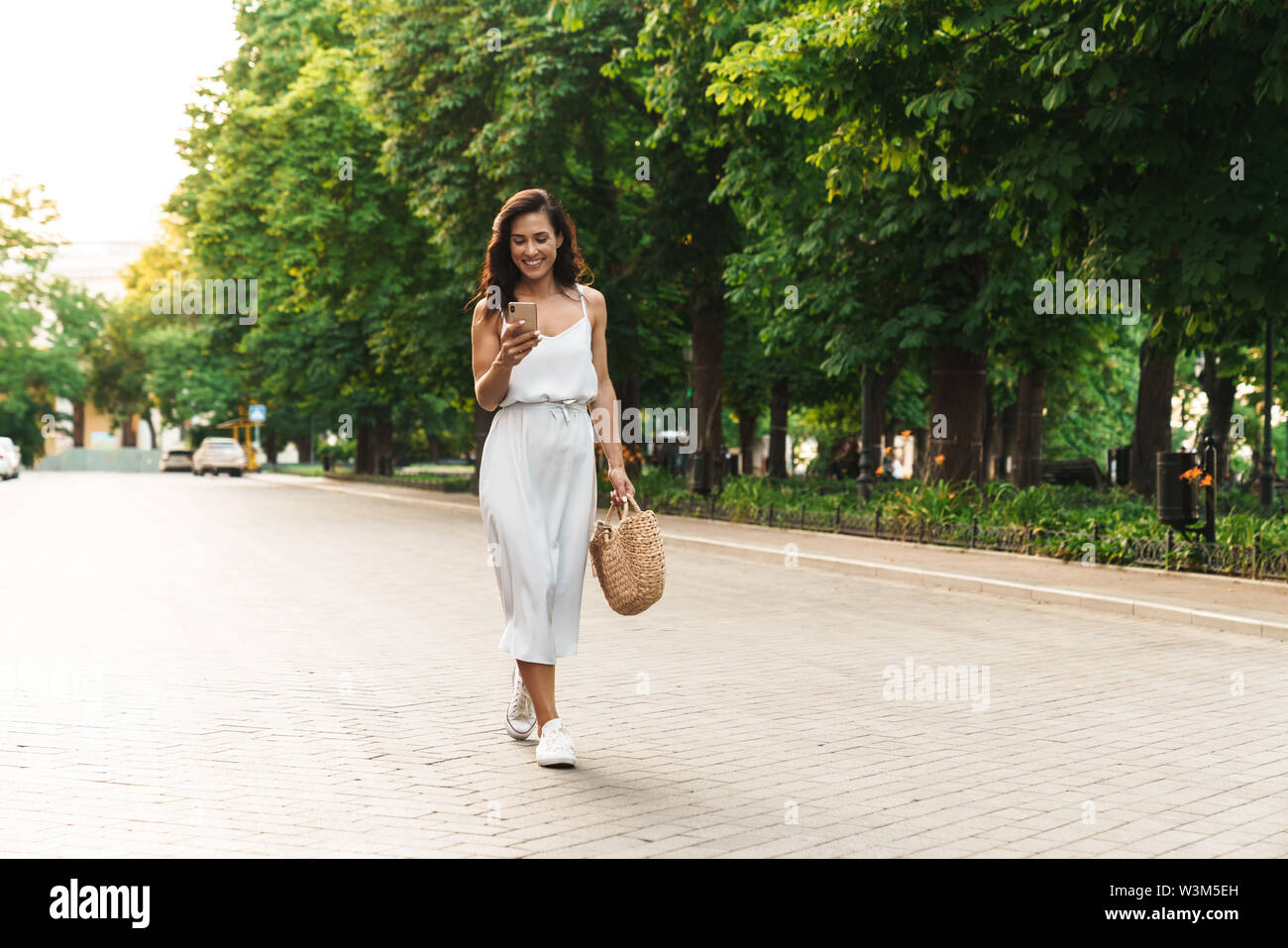 Portrait of cheerful woman in summer dress smiling and holding ...