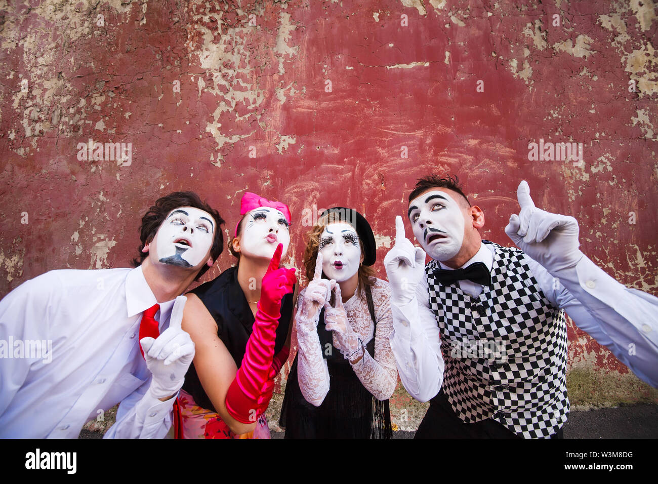 Four mimes point to the top on a red wall Stock Photo - Alamy