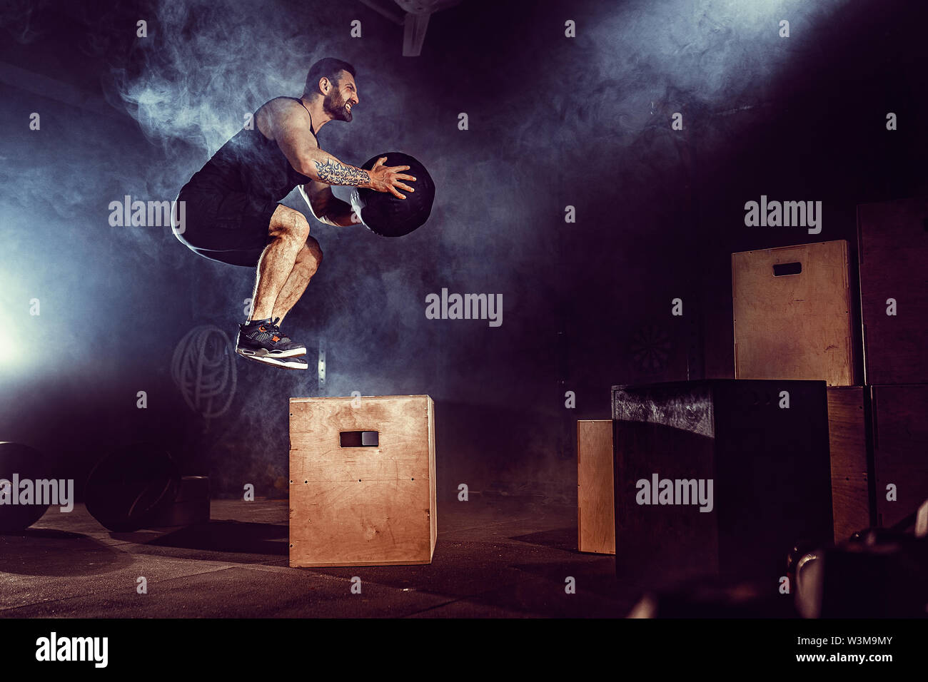 Fit tattoed bearded man jumping onto a box as part of exercise routine ...