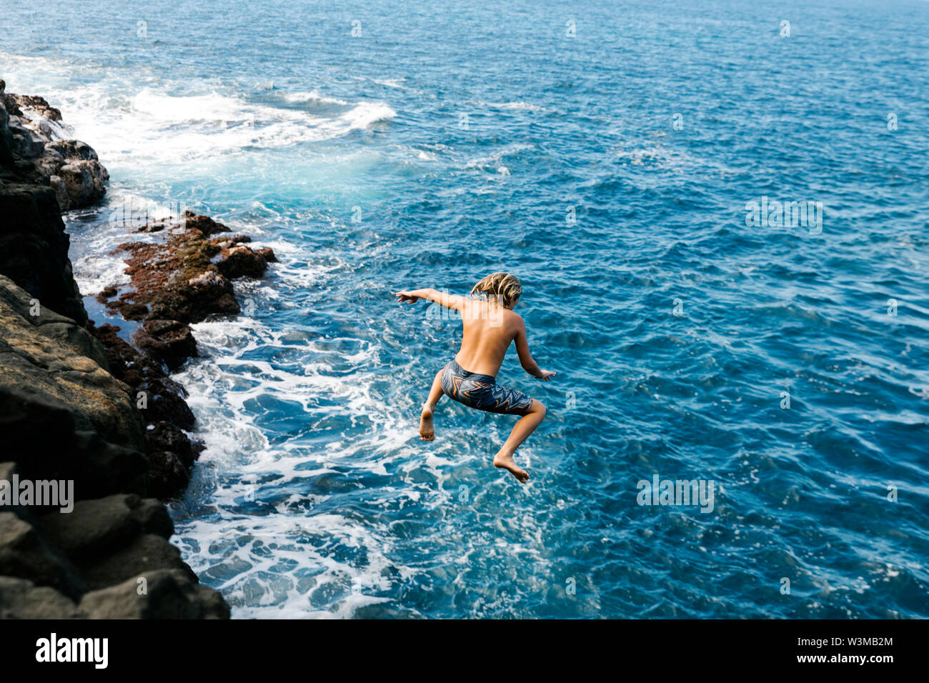 Boy jumping off cliff by sea Stock Photo - Alamy