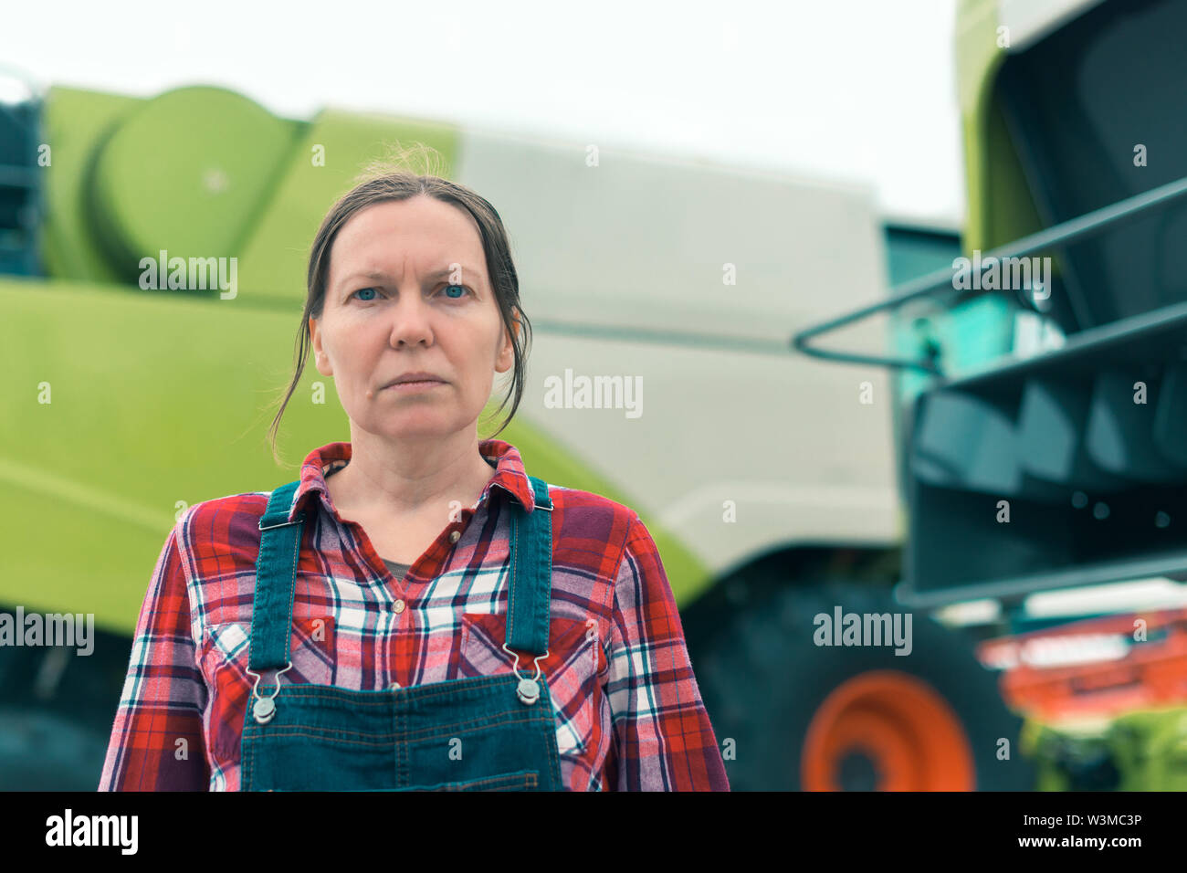 Female farmer posing in front of combine harvester. Serious woman farm ...