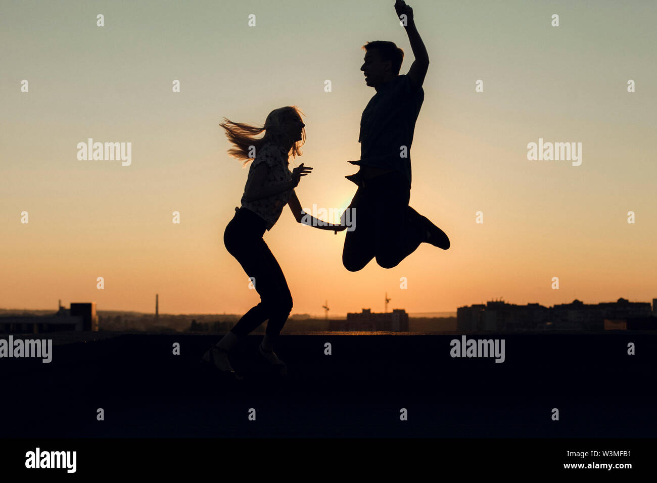 Silhouettes of young couple jumping at sunset Stock Photo - Alamy
