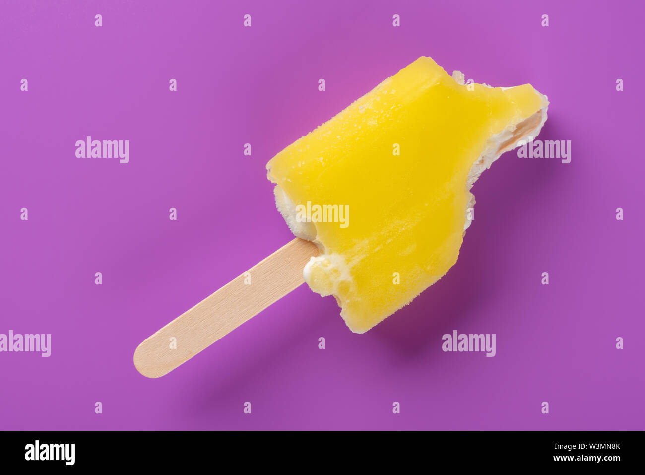 half eaten yellow popsicle on a purple background Stock Photo - Alamy
