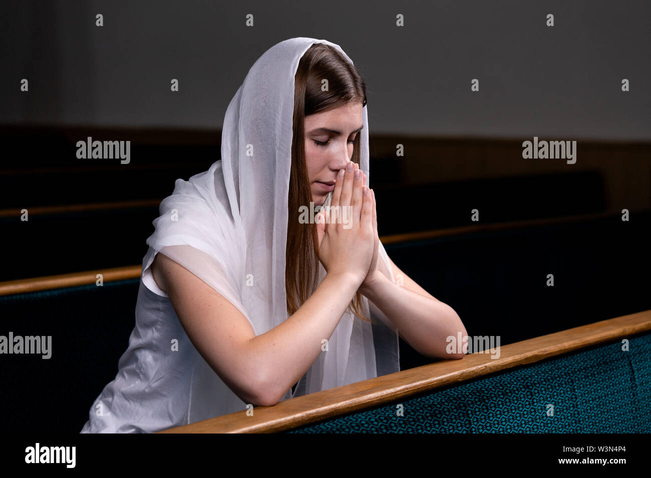 A young modest girl with a handkerchief on her head is sitting in ...