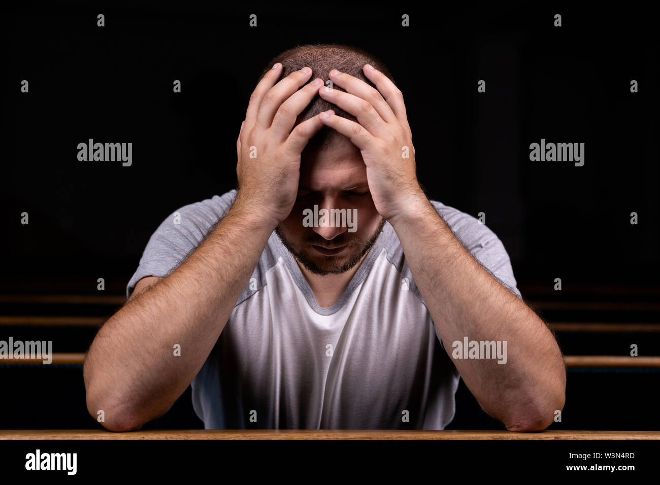 A Sad Christian man in white shirt is sitting and praying with humble ...
