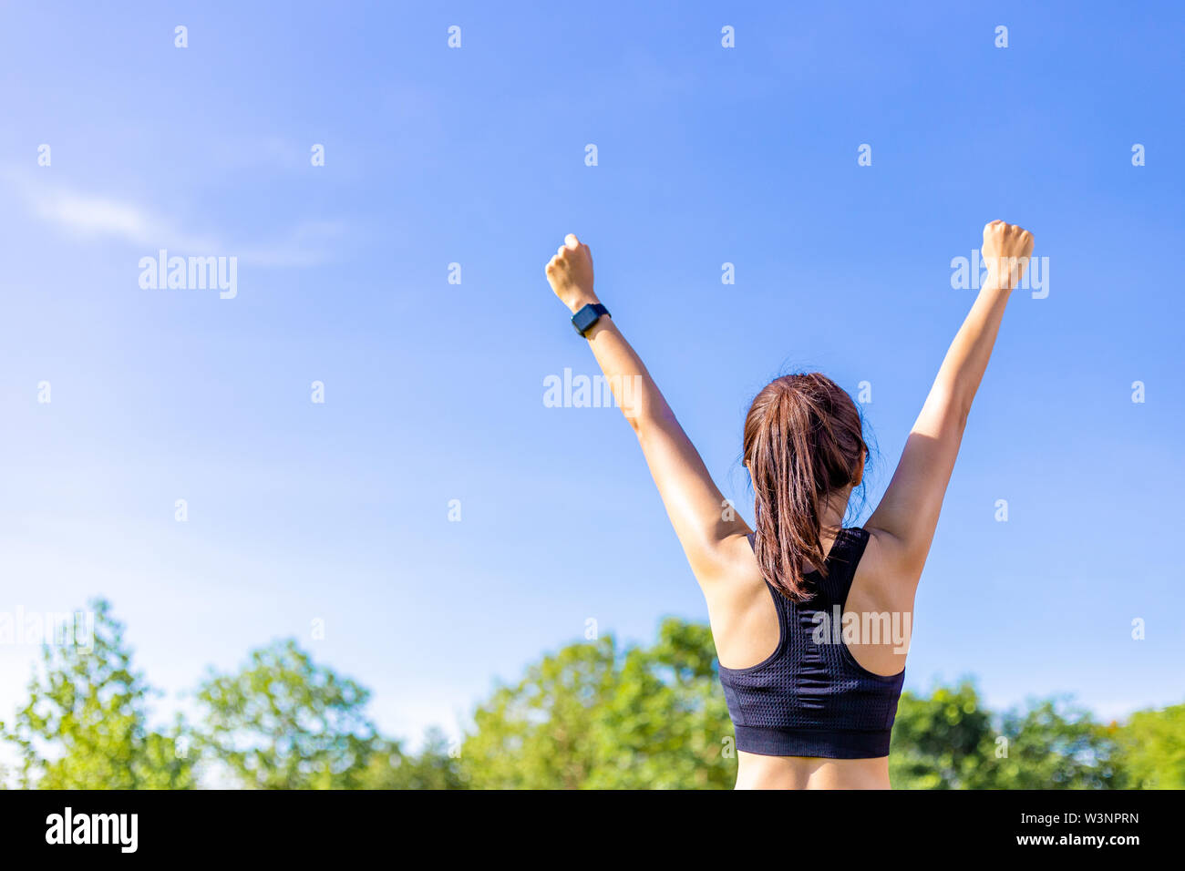 Back view of a woman in stretching up her arms and fists happily at an ...