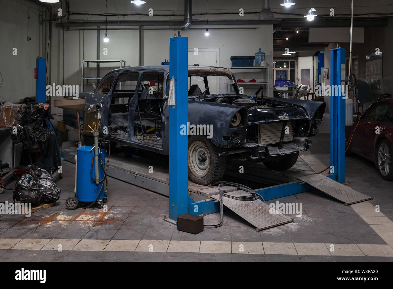 An old classic retro car of black color stands on a blue lift for ...