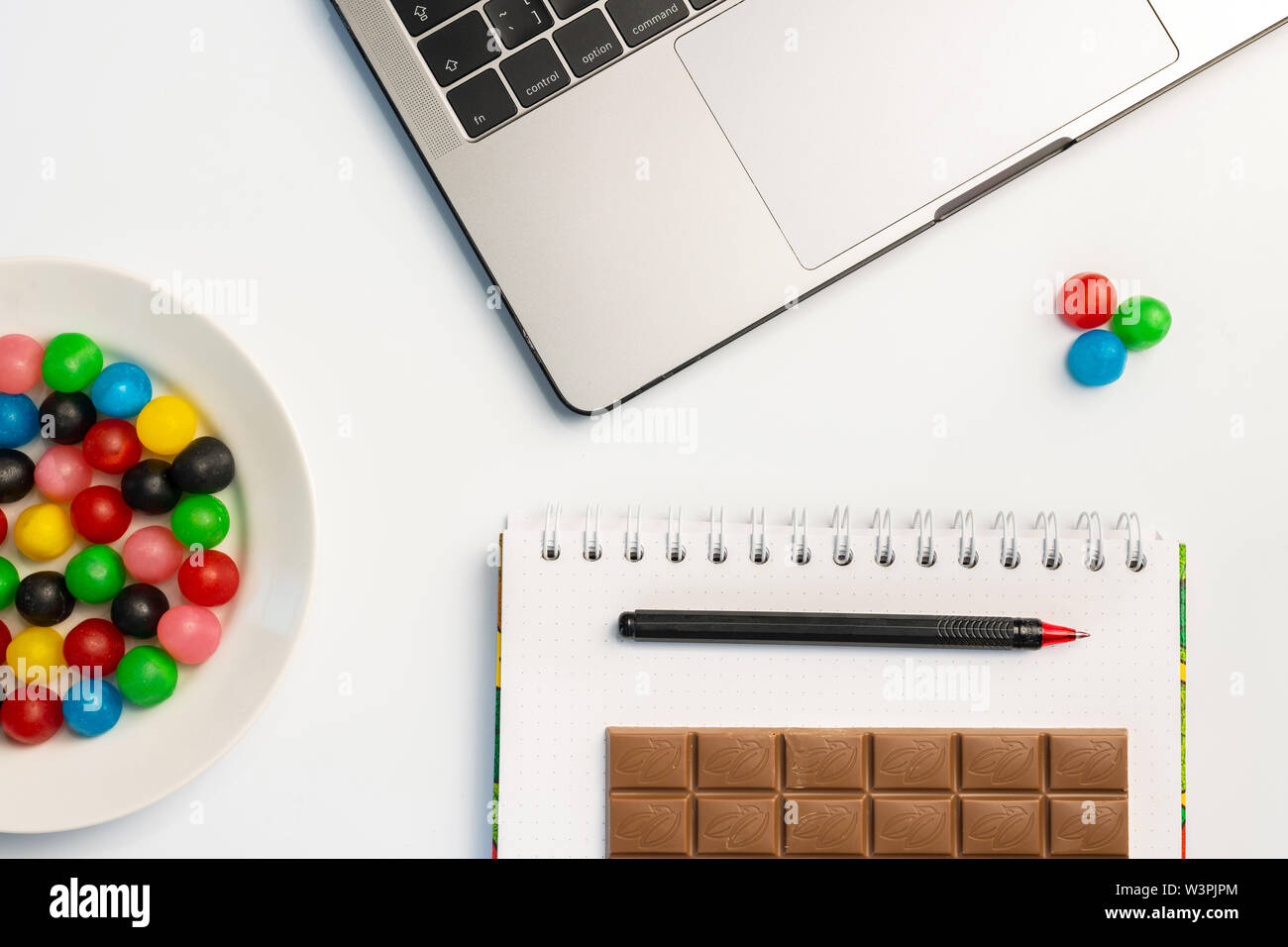 Snacking at work, have a bite concept. Laptop, candy and workbook with ...