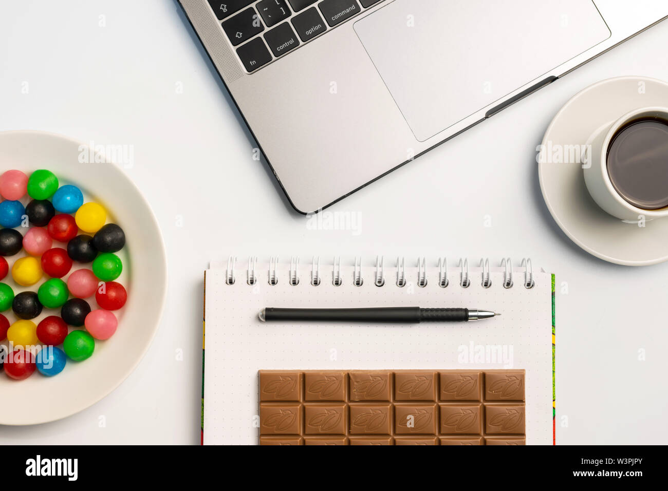 Snacking at work, have a bite concept. Laptop, candy and workbook with ...