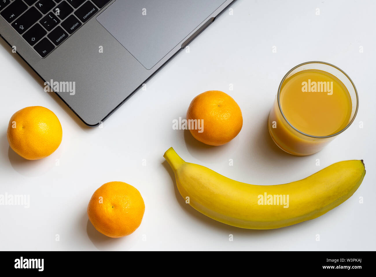 Fruits on workplace. Laptop, banana, mandarins and orange juice on ...