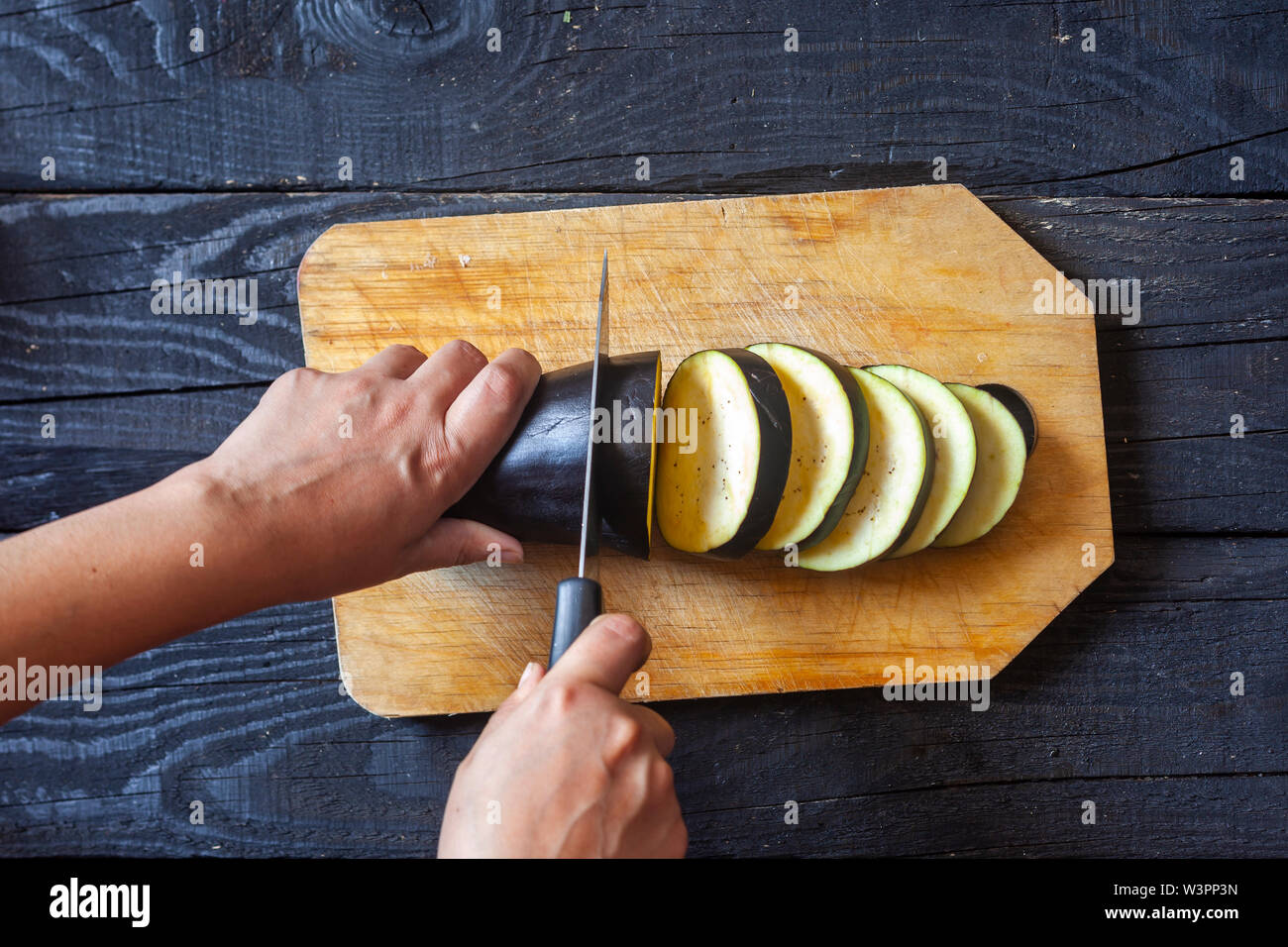 Hand cutting vegetables in kitchen. Female slicing a big eggplant on ...