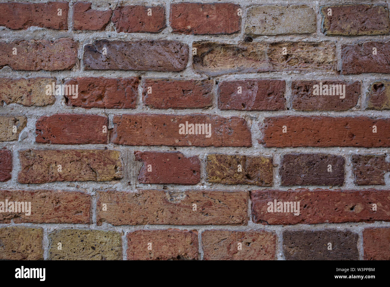 Wall made from red and sometimes colorful bricks of regular shapes and ...