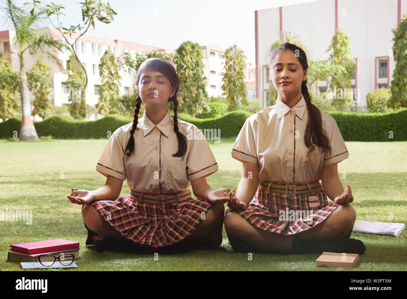 School girls meditating with books kept aside them in the school campus ...