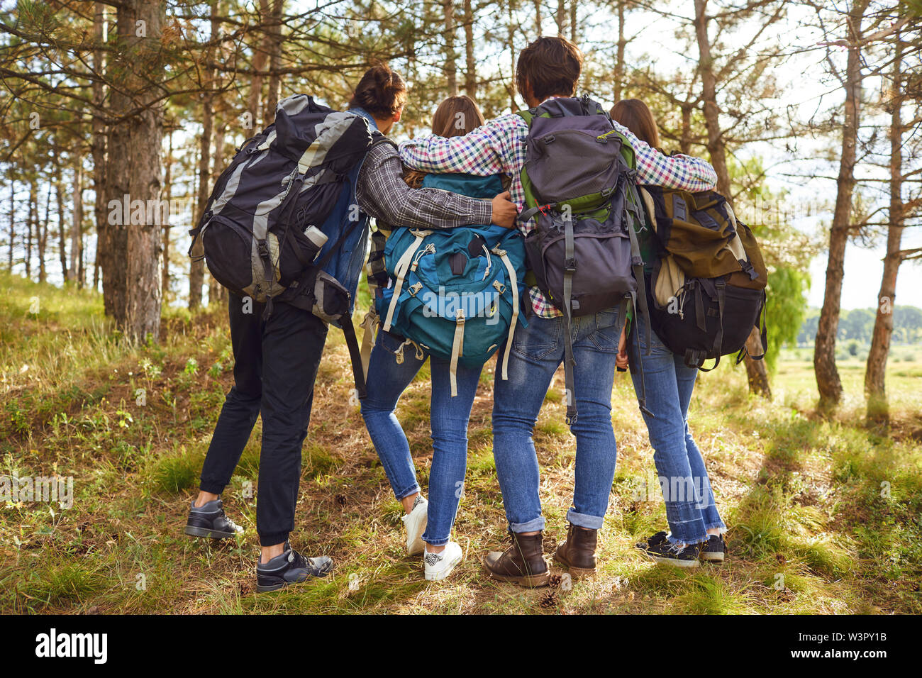 Young people with backpacks stand in the forest from behind. Tourists ...