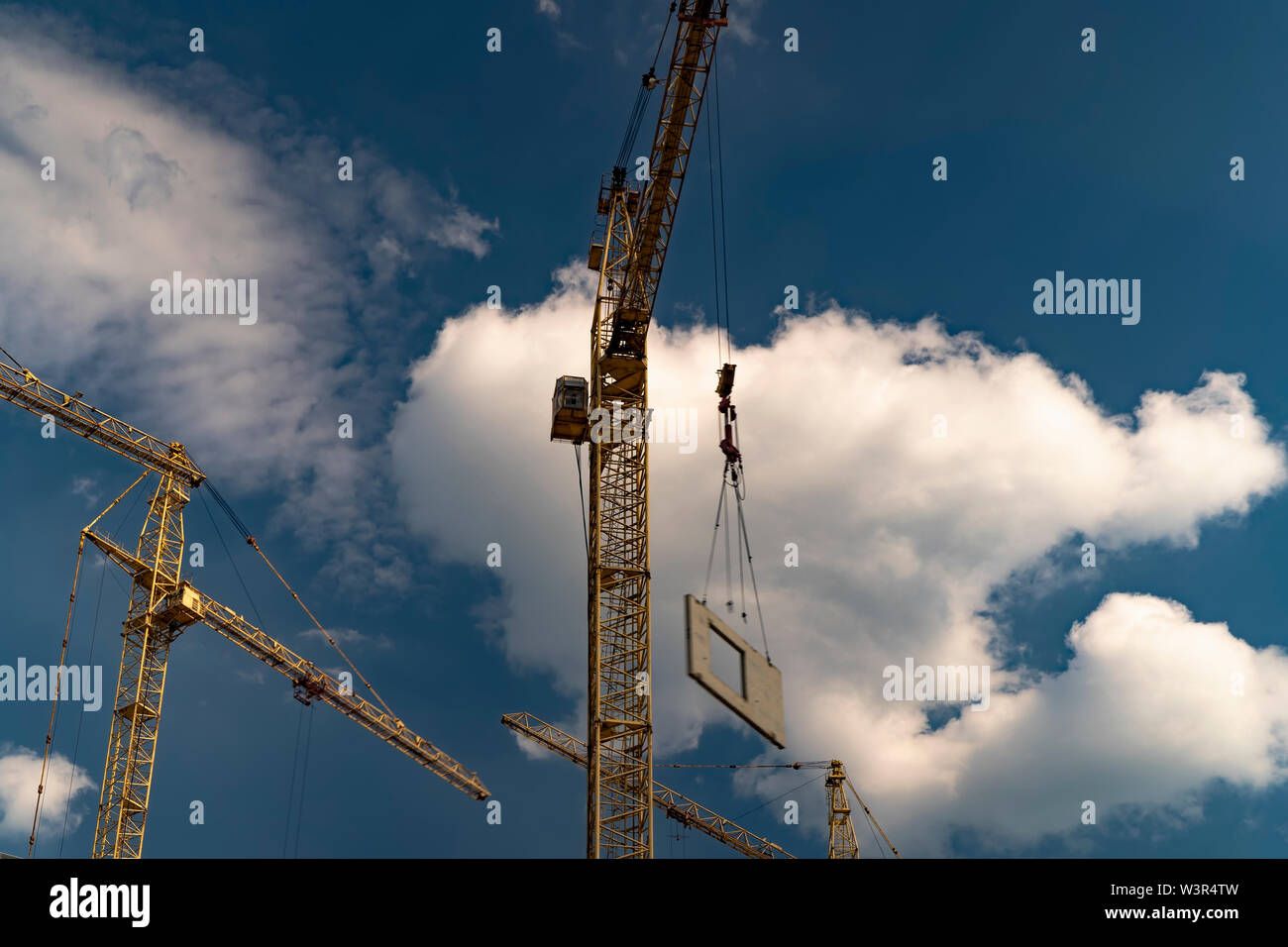 The work of construction cranes on the background of flying clouds ...