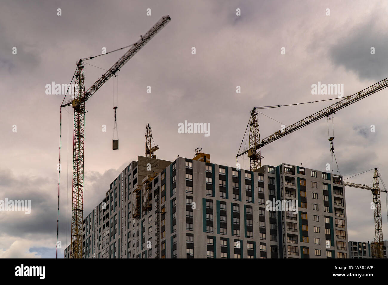 The work of construction cranes on the background of flying clouds ...