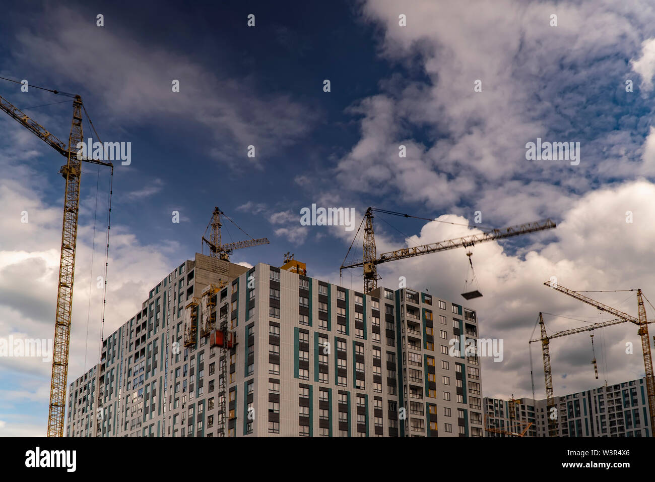 The work of construction cranes on the background of flying clouds ...
