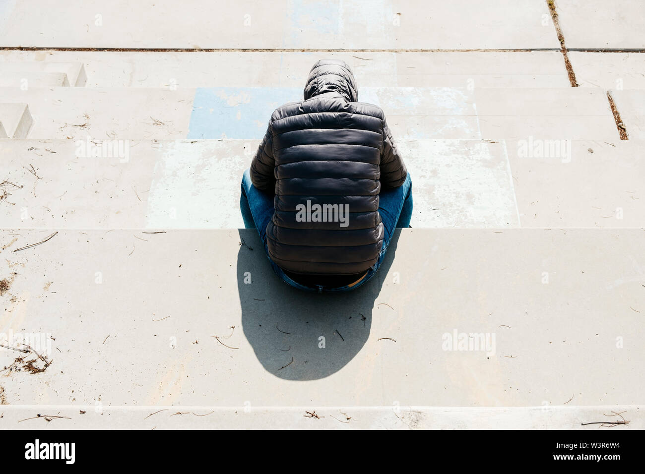 a young caucasian man, seen from behind, wearing jeans and a gray ...