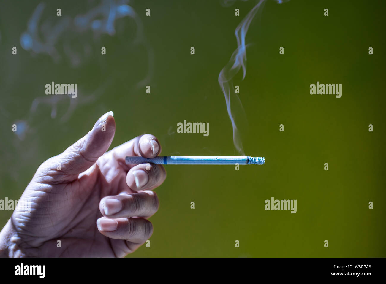 Hand with sigarette smoke on the green background Stock Photo - Alamy
