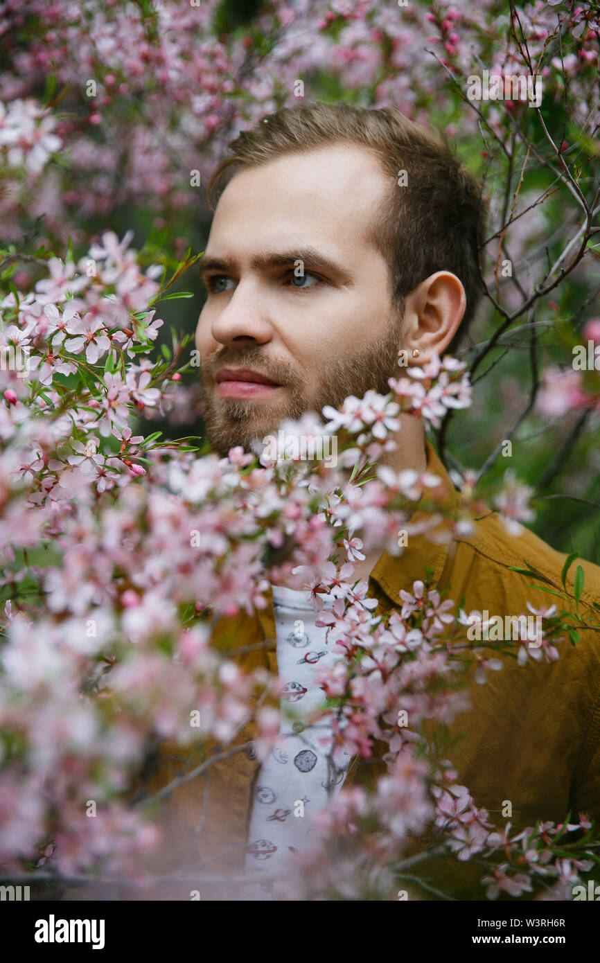 Young cute stylish guy dreams in green and lush pink almond flowers on ...