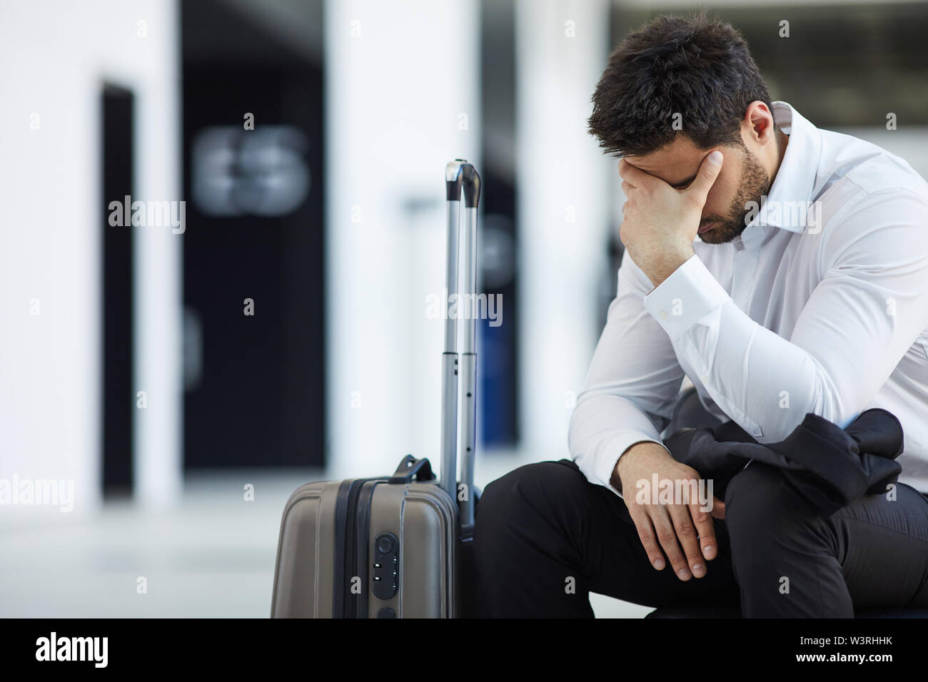 Sad handsome young businessman in white shirt sitting with wheeled ...