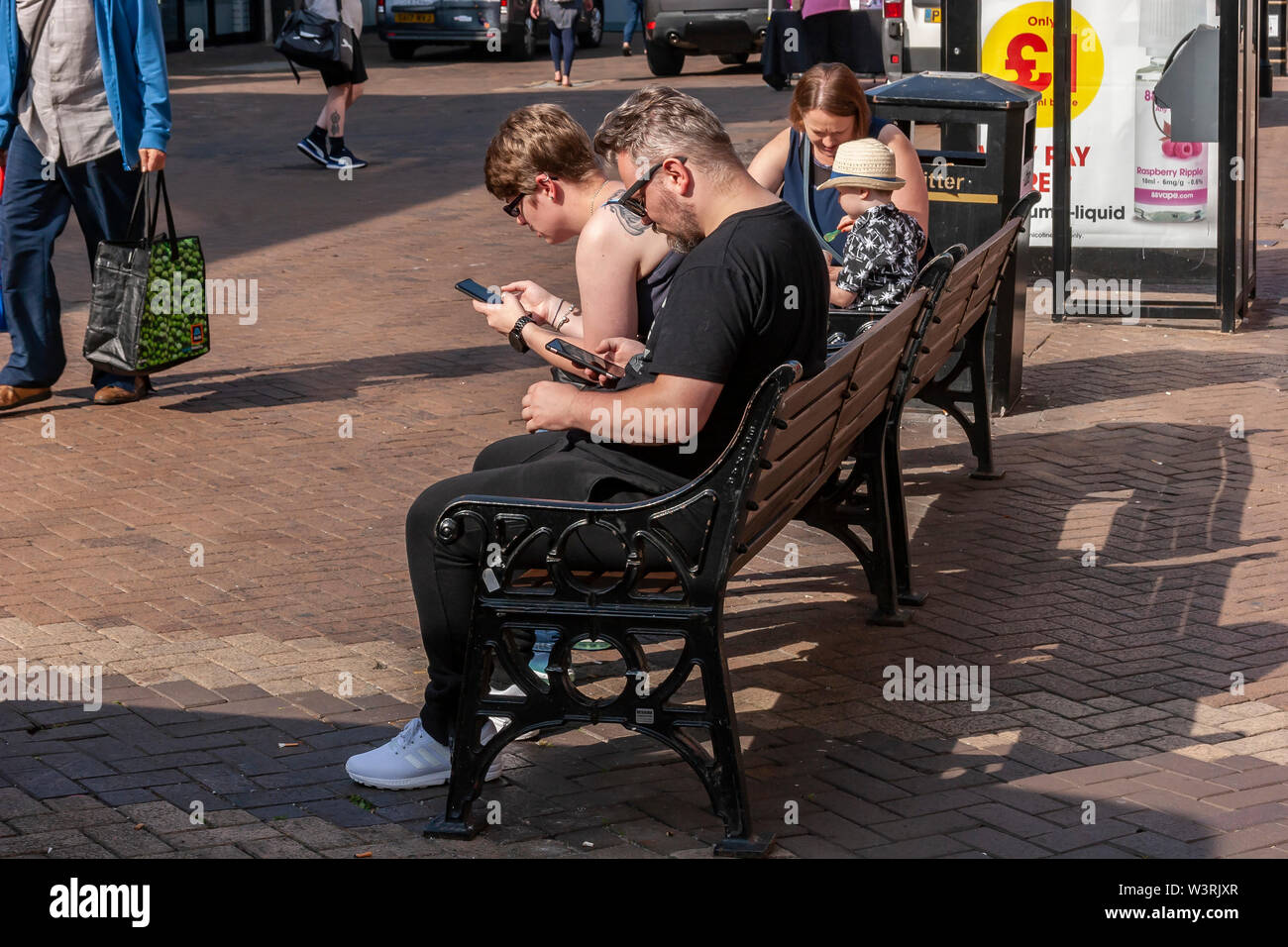two men chilling and on their mobile phones sitting on a bench in ...